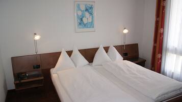 Quarto de hotel com uma cama grande, duas mesinhas de cabeceira, um criado-mudo, um quadro pendurado na parede e uma janela com cortinas.