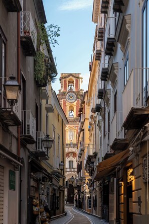 Uma rua estreita ladeada por edifícios, com uma torre do relógio ao longe, e céu limpo.