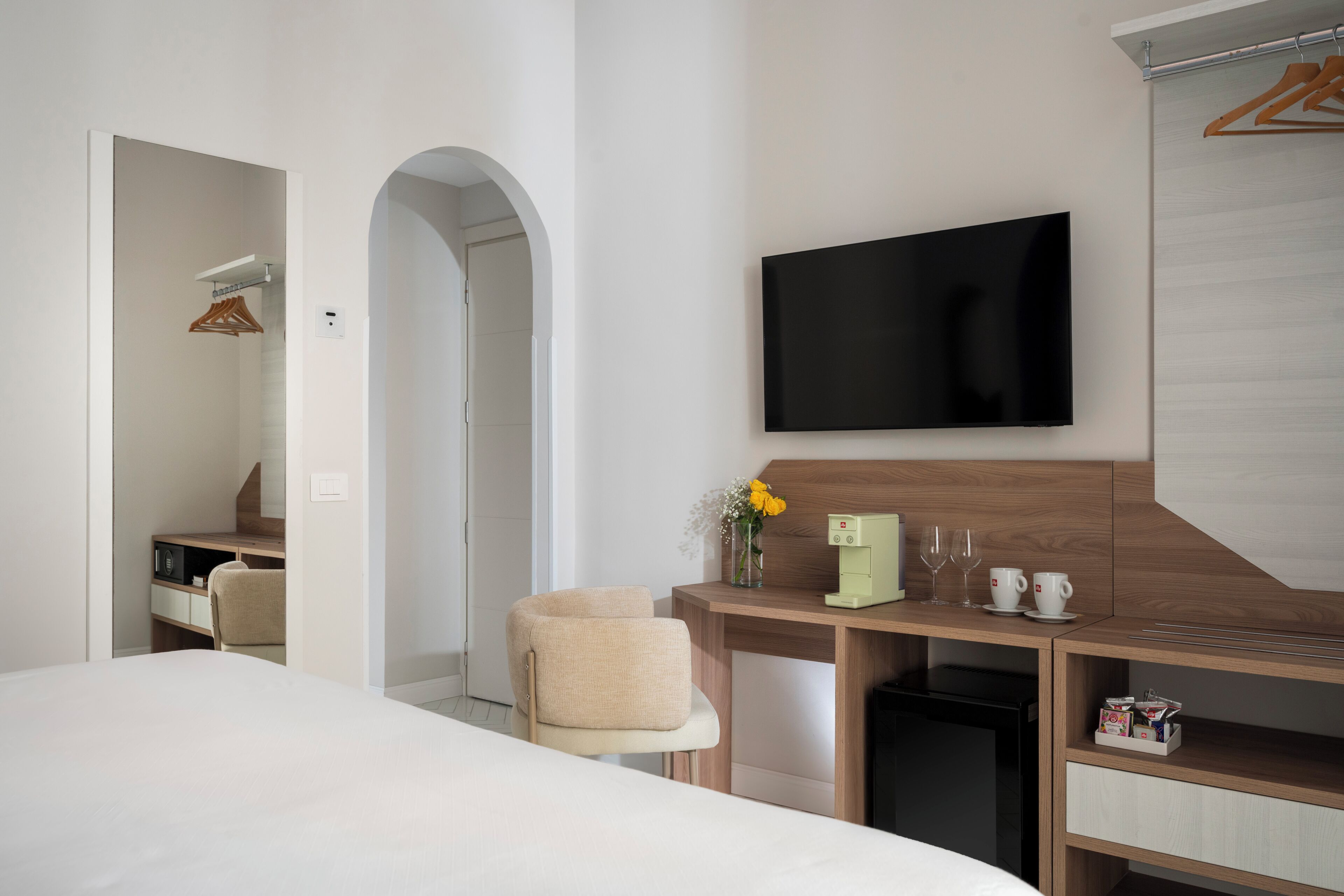 Quarto de hotel com cama, secretária com televisão, cadeira, máquina de café e armário pequeno.