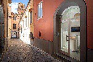 Rua de paralelepípedos estreita que leva a um edifício com uma grande entrada em arco e o número '33' visível na porta.