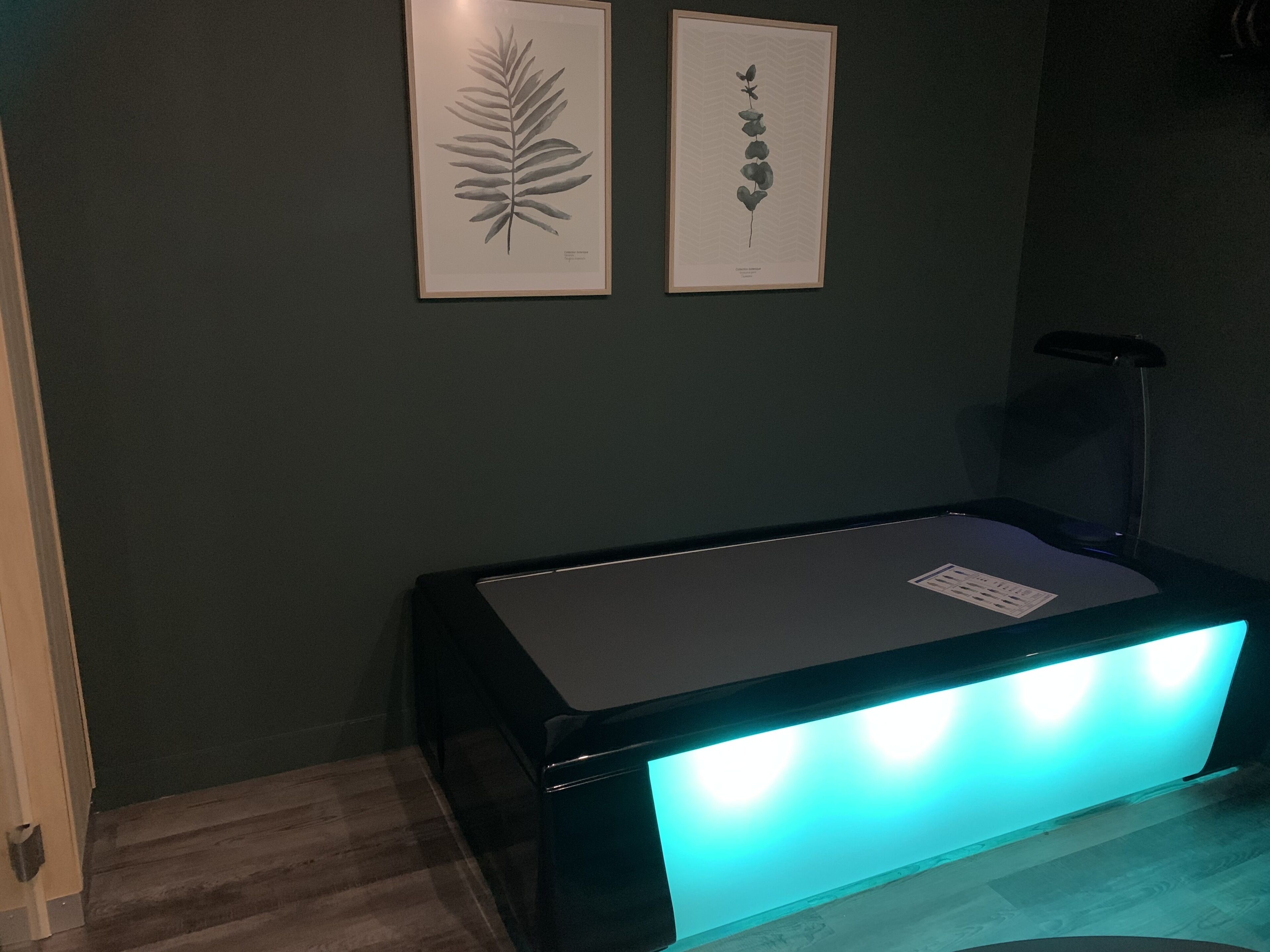Quarto com uma cama, luminária fixada na parede e duas impressões botânicas emolduradas.