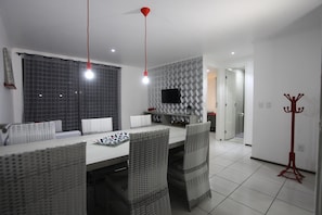 Uma sala de jantar moderna com uma mesa branca, cadeiras cinzas e uma luminária pendente vermelha.