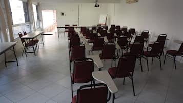 Uma sala de conferências com fileiras de cadeiras vermelhas e mesas, um quadro branco e um projetor.