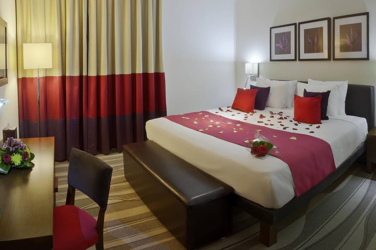Quarto de hotel com cama, mesa de cabeceira, cadeira e escrivaninha com cadeira.