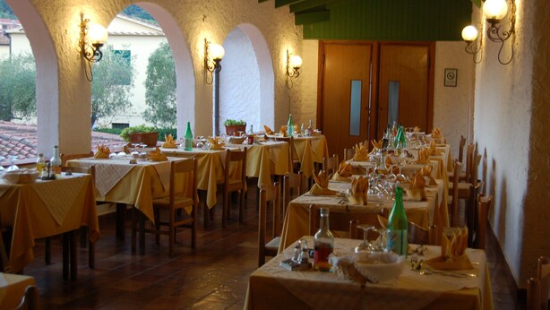 Restaurante com mesas preparadas para refeições, com interior rústico, arcos e iluminação embutida nas paredes.