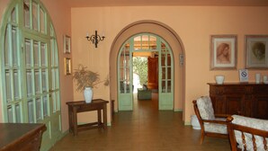 Um corredor com uma porta em arco, um banco de madeira, uma mesa com um vaso e quadros nas paredes.
