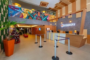 Um lobby de hotel com uma mesa de recepção, um mural colorido e um pinheiro de Natal.
