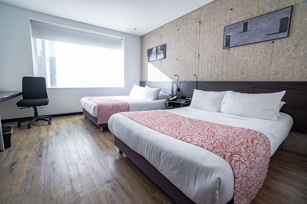 Quarto de hotel com duas camas, uma mesa e uma cadeira.