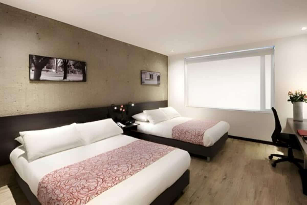 Quarto de hotel com duas camas, uma mesa, uma cadeira e uma janela.