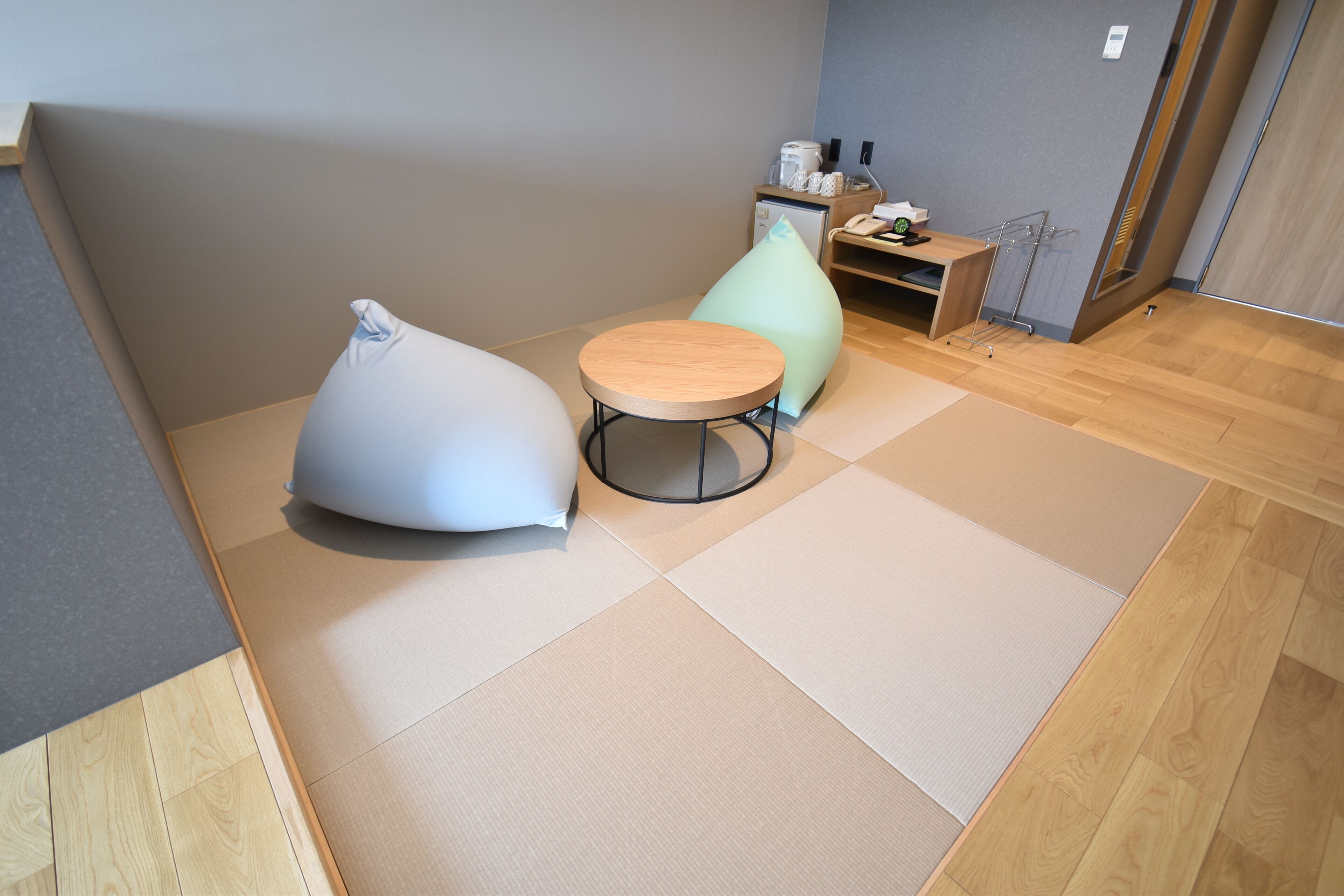 Um quarto com piso de tatame, uma mesa de madeira redonda e duas poltronas de feijão.