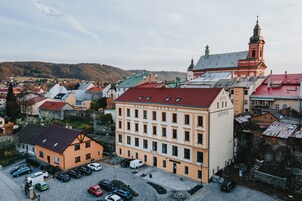 Um hotel com telhado vermelho e uma torre do relógio, cercado por outros edifícios e uma paisagem montanhosa ao fundo.