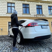 Um Tesla branco estacionado em frente a um edifício com uma placa que diz 'HOTEL'.