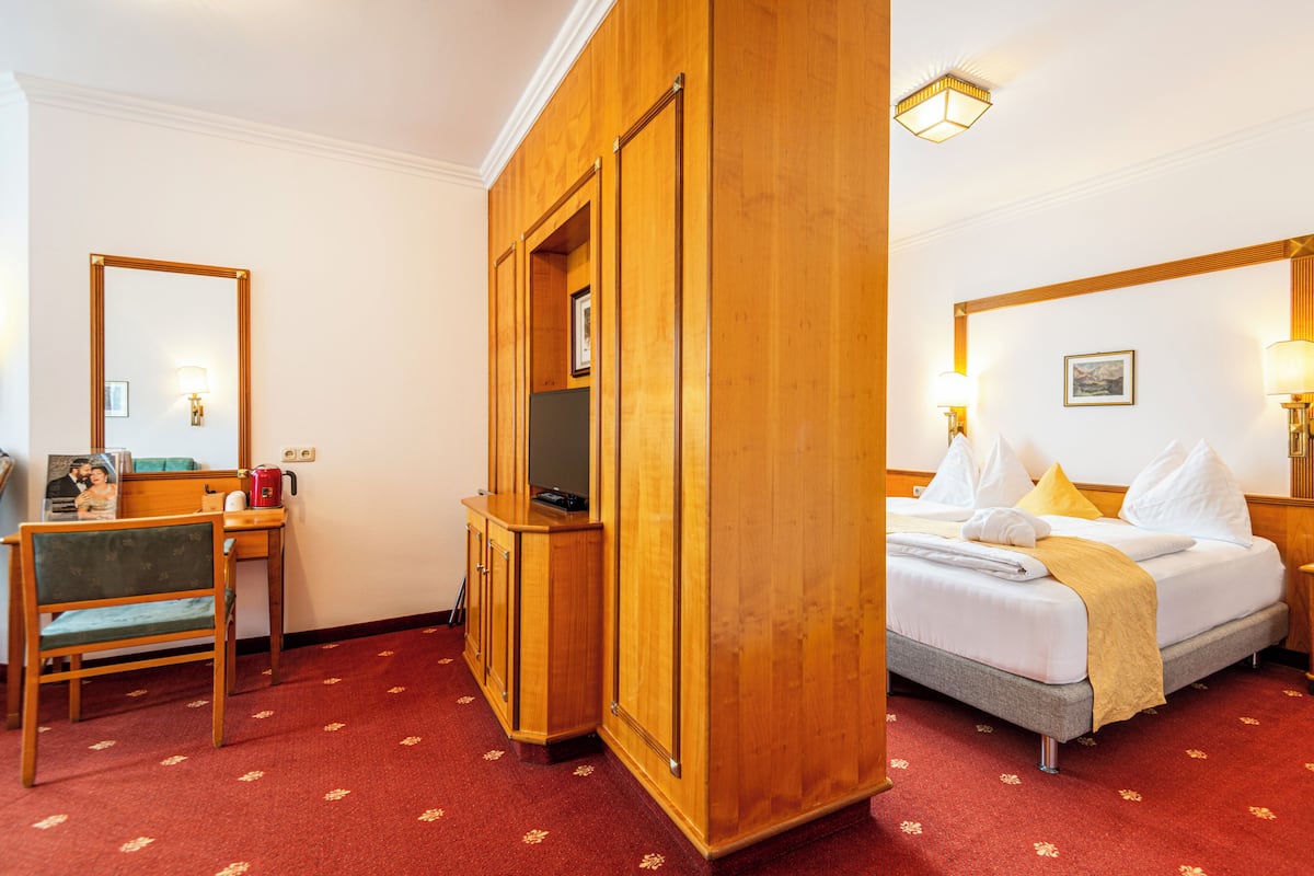 Quarto de hotel com cama, escrivaninha, cadeira, guarda-roupa e espelho.