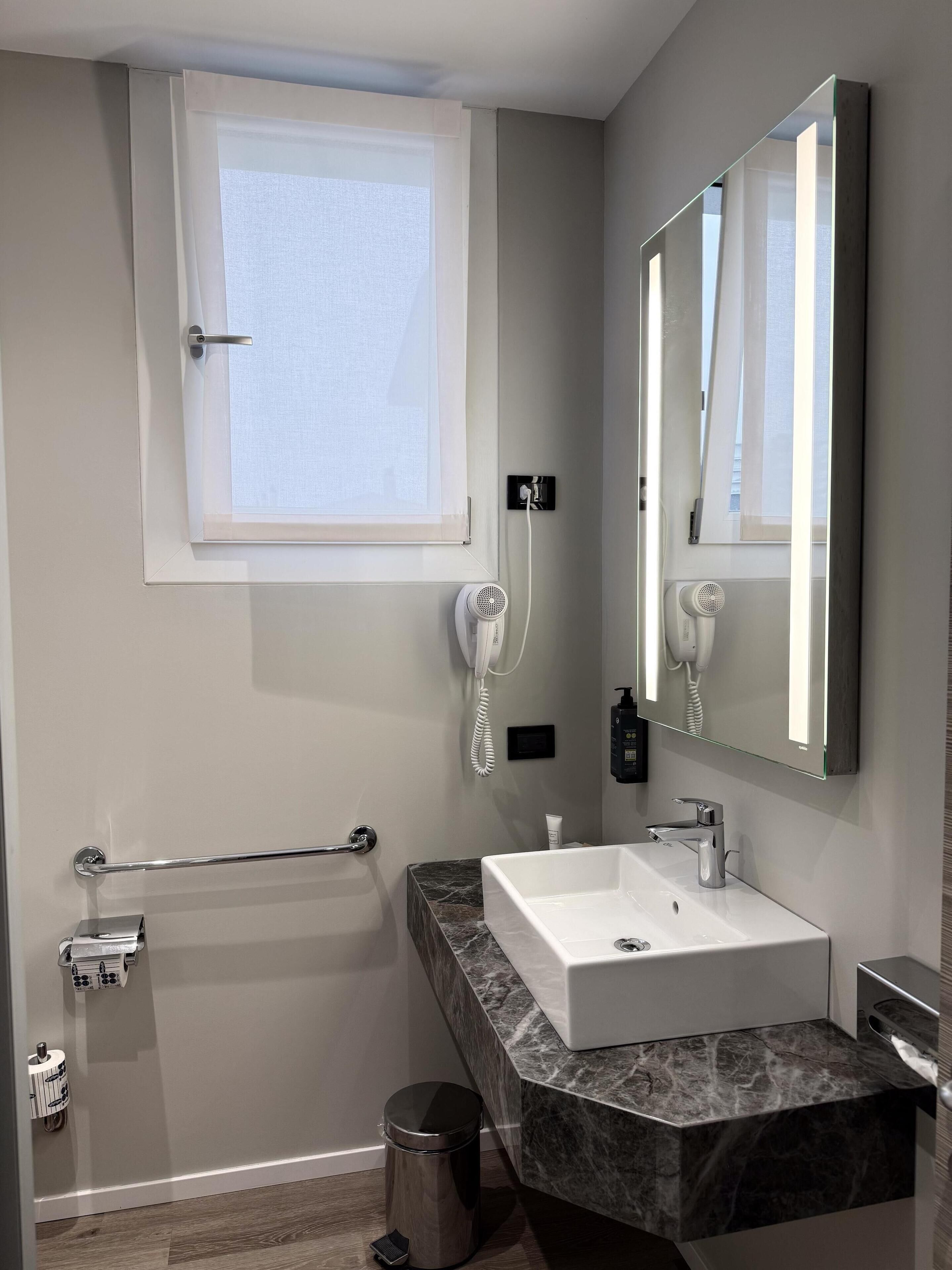 Uma casa de banho moderna com lavatório embutido, um espelho grande, uma janela e um porta-toalhas.