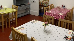 Uma área de refeições com uma mesa posta para quatro pessoas, uma estante com utensílios de cozinha e um quadro na parede.