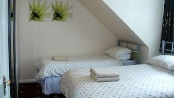 Quarto com duas camas, teto inclinado e porta para outro cômodo.