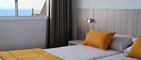 Quarto de hotel com uma cama, mesa de cabeceira, luminária e vista para o mar pela janela.
