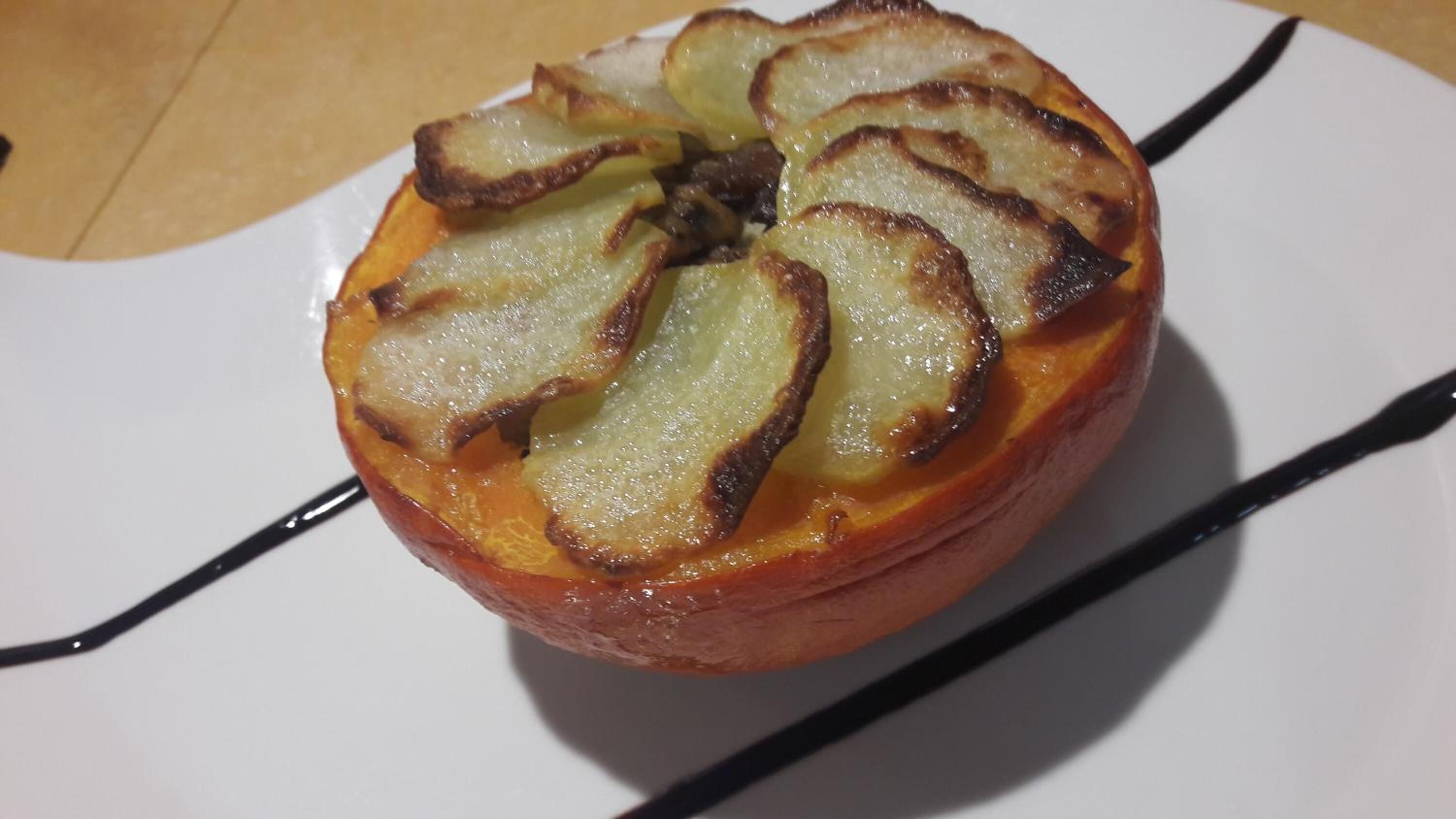 Uma sobremesa com cobertura caramelizada, possivelmente uma torta ou bolo, em um prato branco com molho escuro escorrido ao redor.