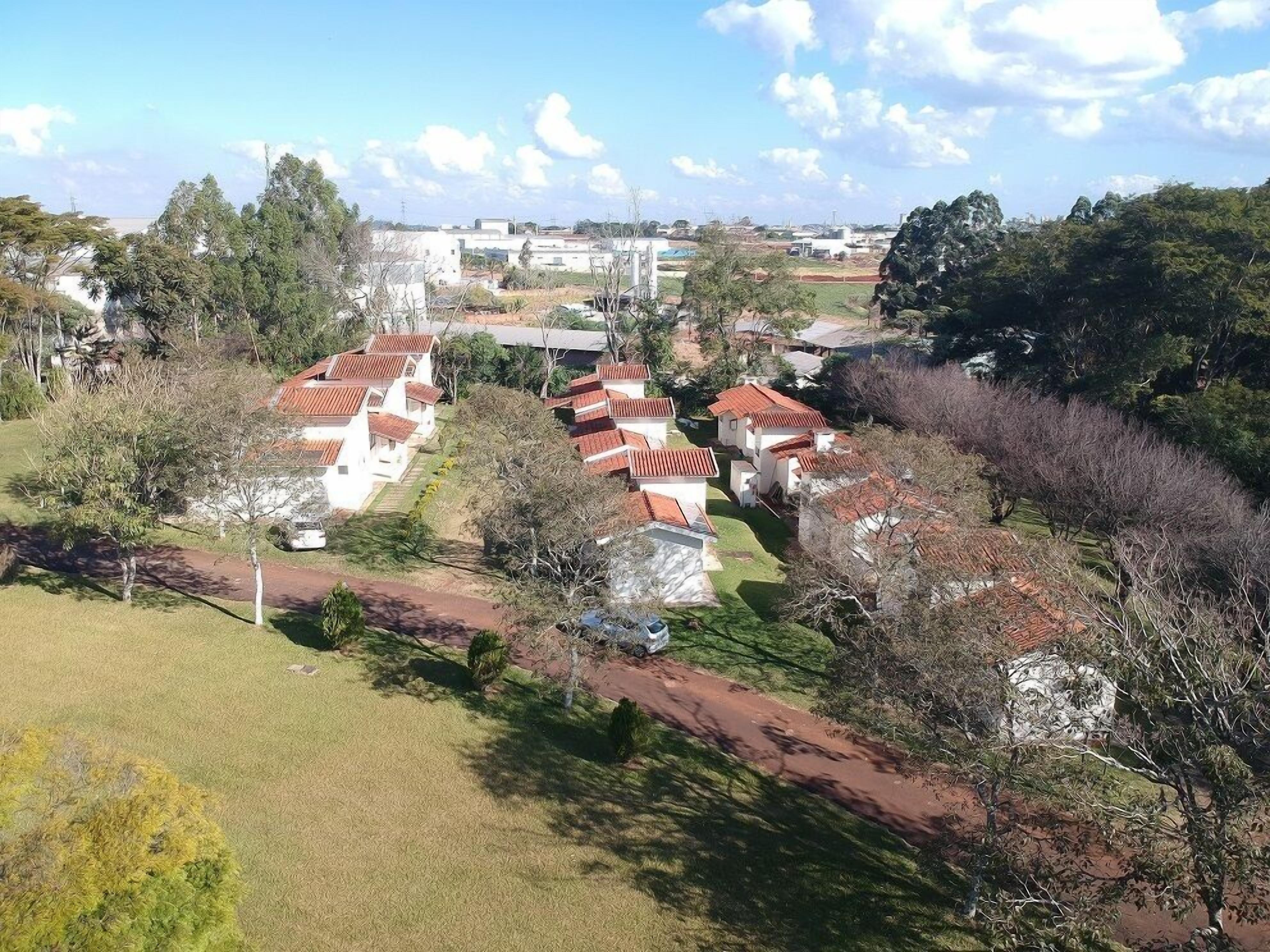 Área residencial com casas e telhados vermelhos, cercada por vegetação e árvores.