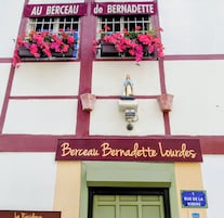 Um edifício com uma placa que diz 'Au Berceau de Bernadette' e uma estátua de Bernadette.
