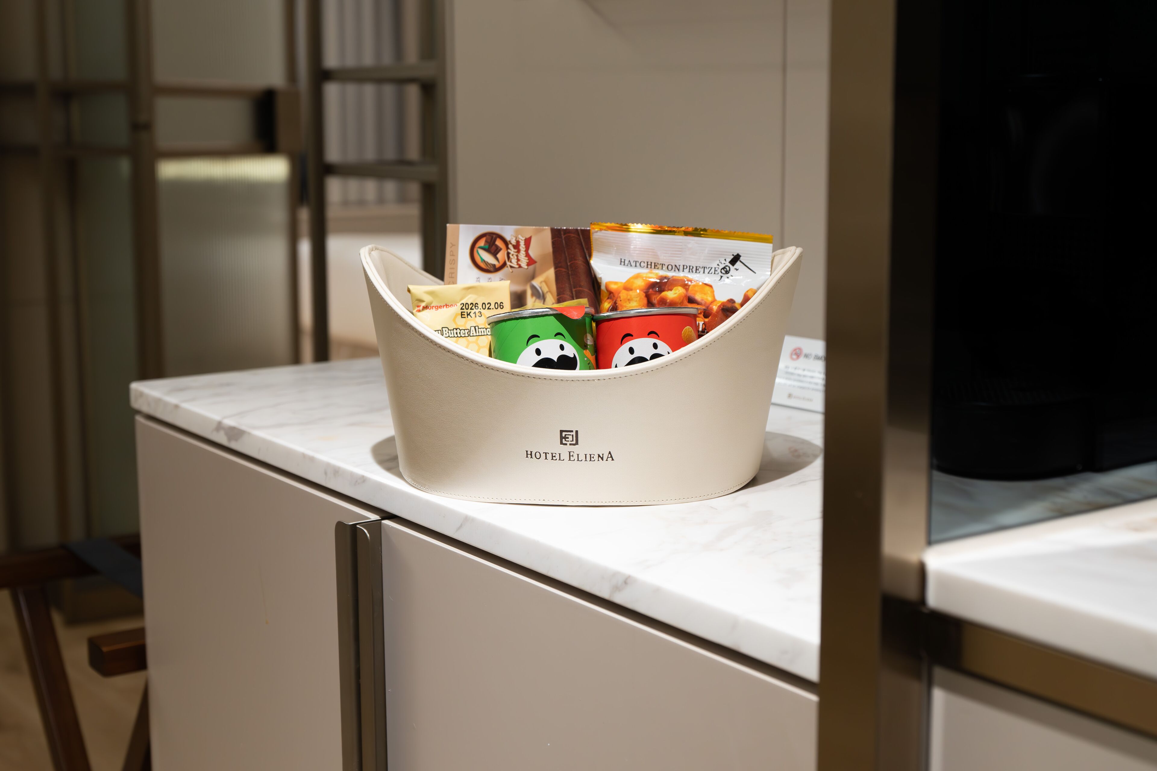Um minibares branco com uma tigela branca contendo diversos petiscos, incluindo uma lata de cerveja de manteiga e uma lata de pretzels Hatcheton.