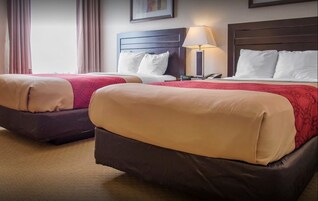 Quarto de hotel com duas camas, cada uma com cabeceira, mesa de cabeceira com abajur, e vista para a cidade pela janela.
