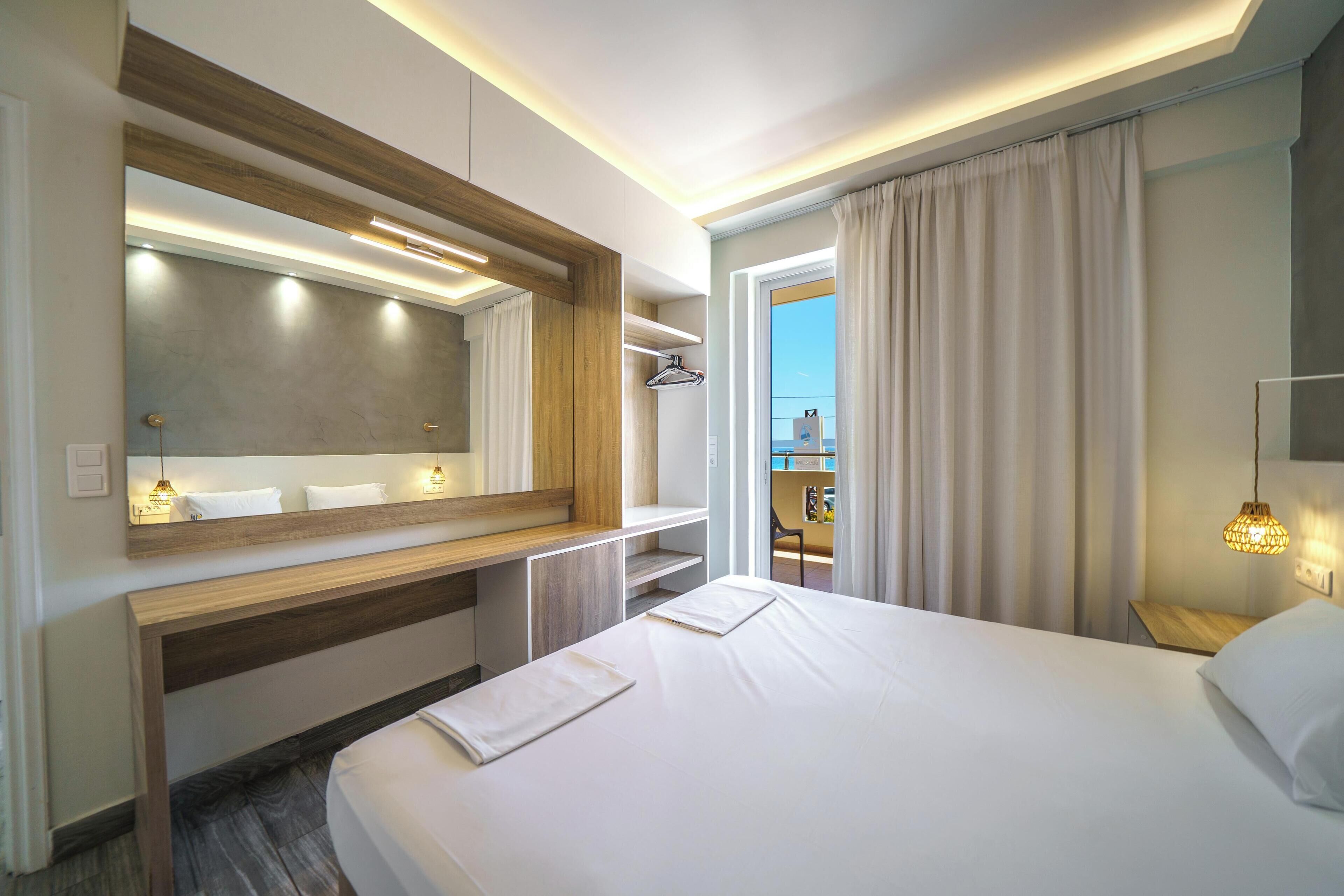 Quarto de hotel moderno com uma cama grande, uma escrivaninha de madeira, um espelho e vista para a varanda.