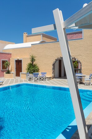 Piscina azul límpida com espreguiçadeiras e um muro de pedra ao fundo.