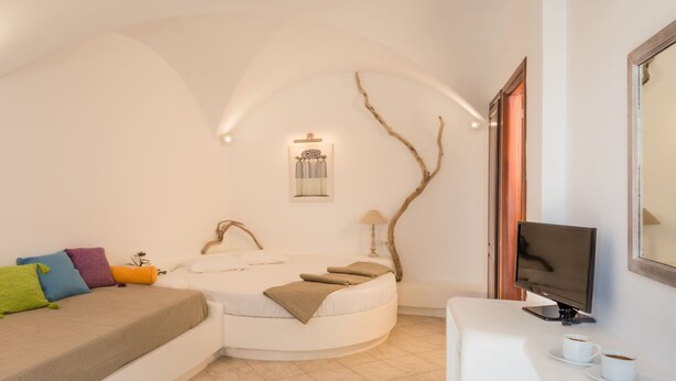 Quarto moderno com cama curva, televisão e uma pequena mesa com chávenas.