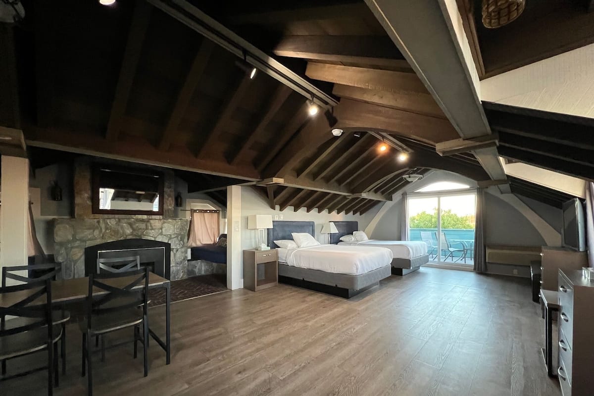 Um amplo quarto no estilo loft, com uma cama grande, uma área de refeições com cadeiras e uma lareira de pedra.