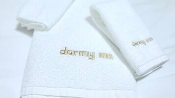 Toalha branca dobrada com a inscrição "dormy inn" bordada em dourado.