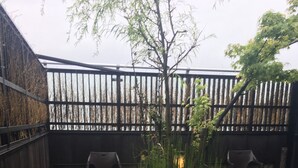 Um pátio com piso de pedra e um pequeno lago, rodeado por uma cerca de metal preto e plantas de bambu.