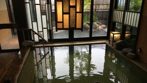 Piscina interior com água cristalina, rodeada por um deck de madeira e vista para um jardim.
