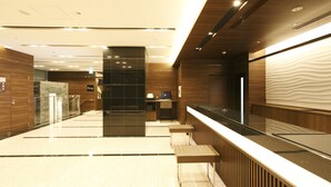 Um lobby moderno de hotel com balcão de recepção, área de estar e um grande painel digital.