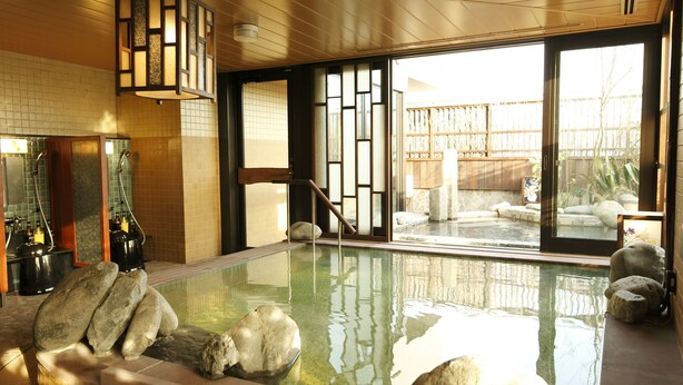 Uma onsen japonesa tradicional com interior em madeira, uma nascente quente de pedra e vista para o jardim exterior.