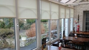 Um restaurante com janelas amplas, mesas e cadeiras de madeira.
