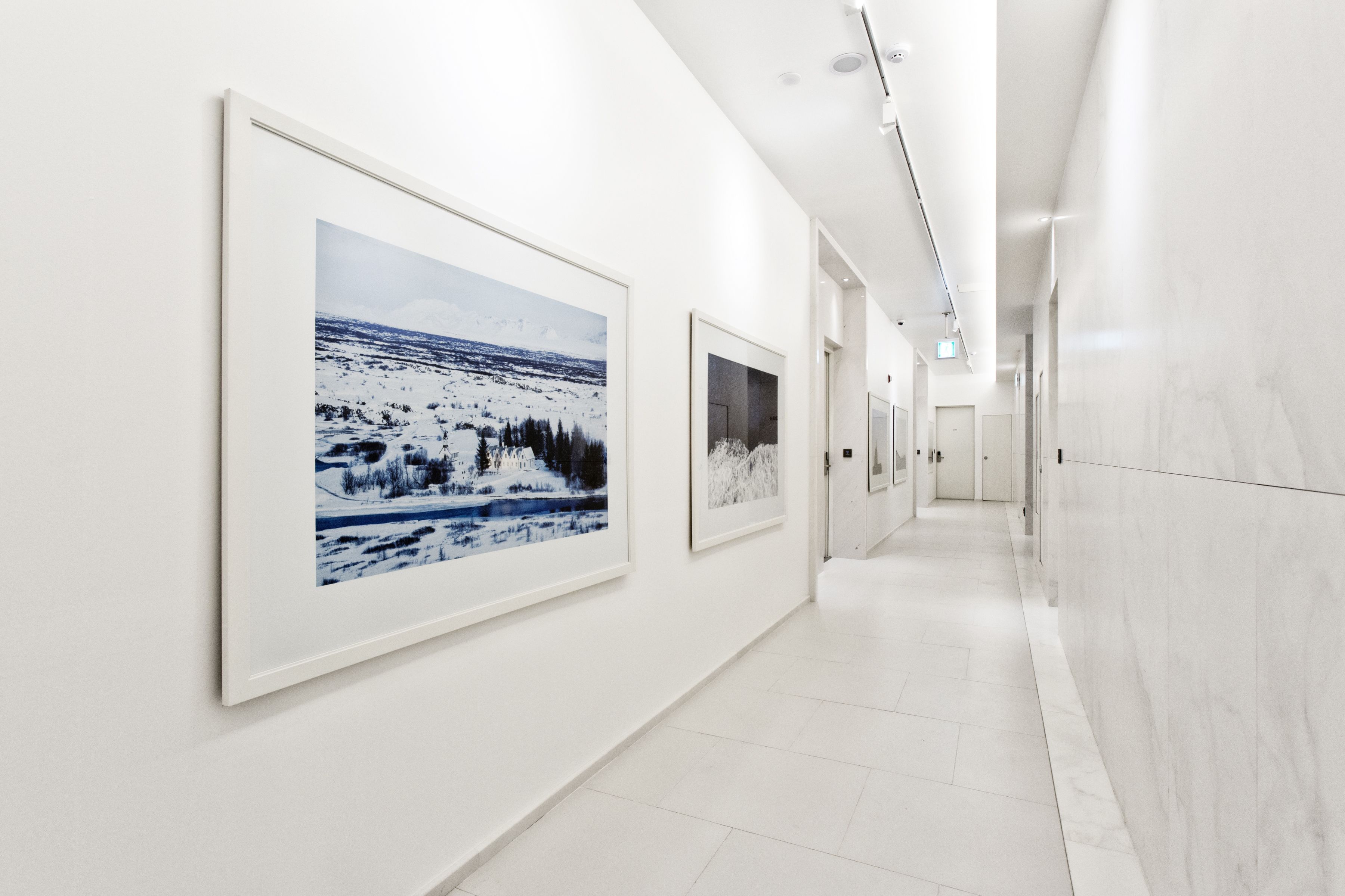 Um corredor com fotografias emolduradas nas paredes, chão de azulejos brancos e luminária de teto moderna.