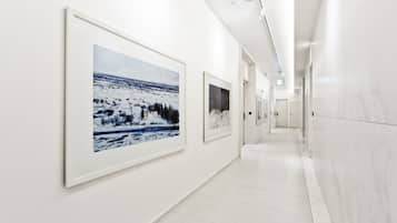 Um corredor com fotografias emolduradas nas paredes, chão de azulejos brancos e luminária de teto moderna.