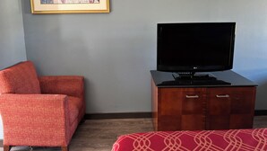 Um quarto com um sofá vermelho estampado, uma televisão sobre um móvel de madeira e um quadro abstrato emoldurado na parede.
