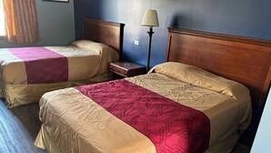 Duas camas de solteiro com cabeceiras de madeira, um criado-mudo e um abajur em um quarto com paredes azuis.