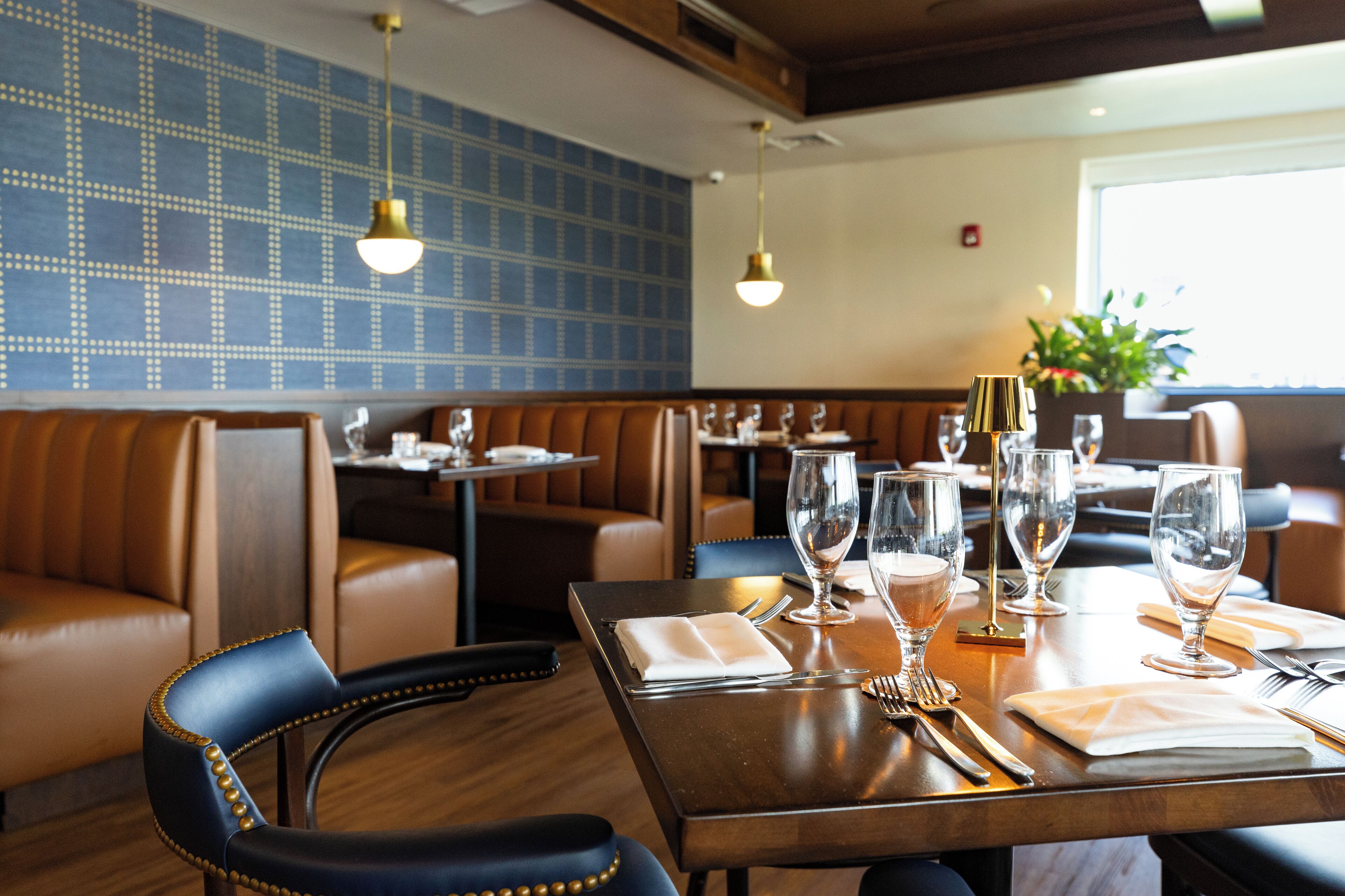 Interior de restaurante com cabines, mesas preparadas para refeições e luminárias pendentes.