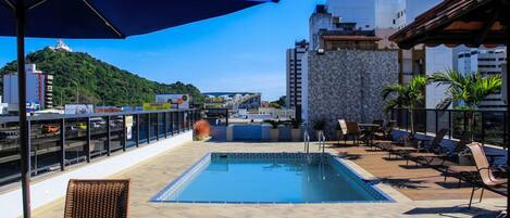 Área de piscina no terraço, vista para uma colina e edifícios.