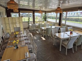 Restaurante com mesas ao ar livre, cadeiras de vime e flores amarelas sobre as mesas.