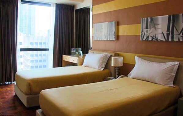 Quarto de hotel com duas camas, mesa de cabeceira, abajur e janela com cortinas.
