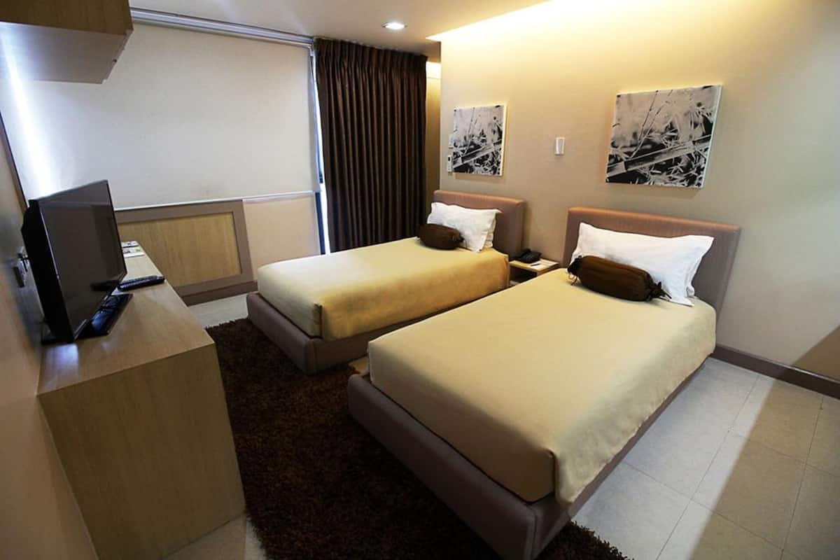 Quarto de hotel com duas camas, uma escrivaninha com um computador e obras de arte nas paredes.
