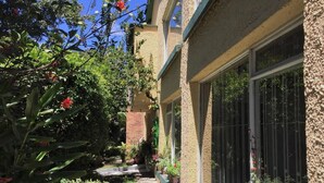 Um edifício com fachada de tijolos, janelas amplas e um jardim com diversas plantas e flores.
