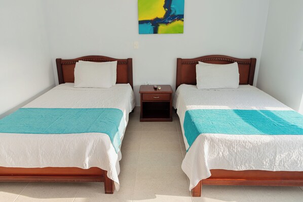 Quarto com duas camas, cada uma com cabeceira de madeira, mesa de cabeceira pequena e criado-mudo.