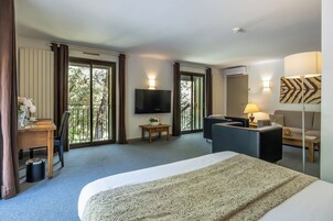Quarto de hotel com cama, escrivaninha, poltrona, sofá, televisão e janela com cortinas.