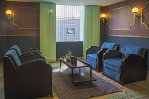 Um quarto com sofá de madeira escura, uma mesinha de centro e um tapete com padrão verde.