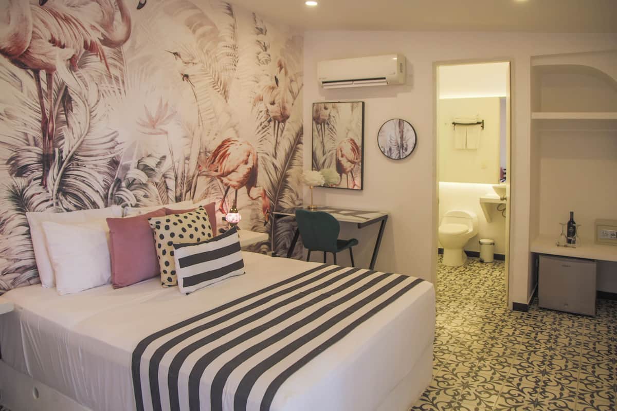 Quarto de hotel com cama, escrivaninha e banheiro visível por uma porta aberta.